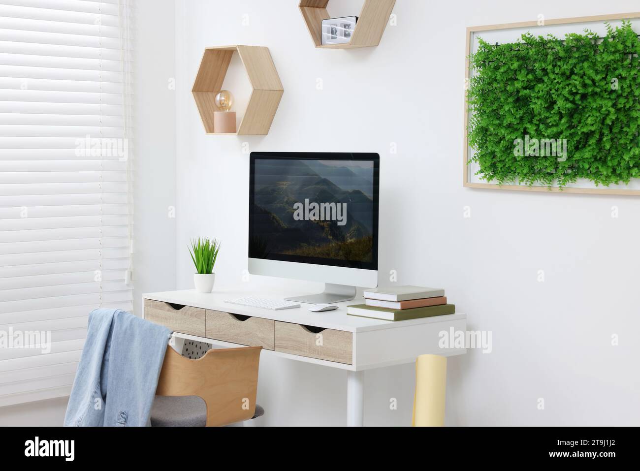 Green artificial plant wall panel and desk with computer in light room ...
