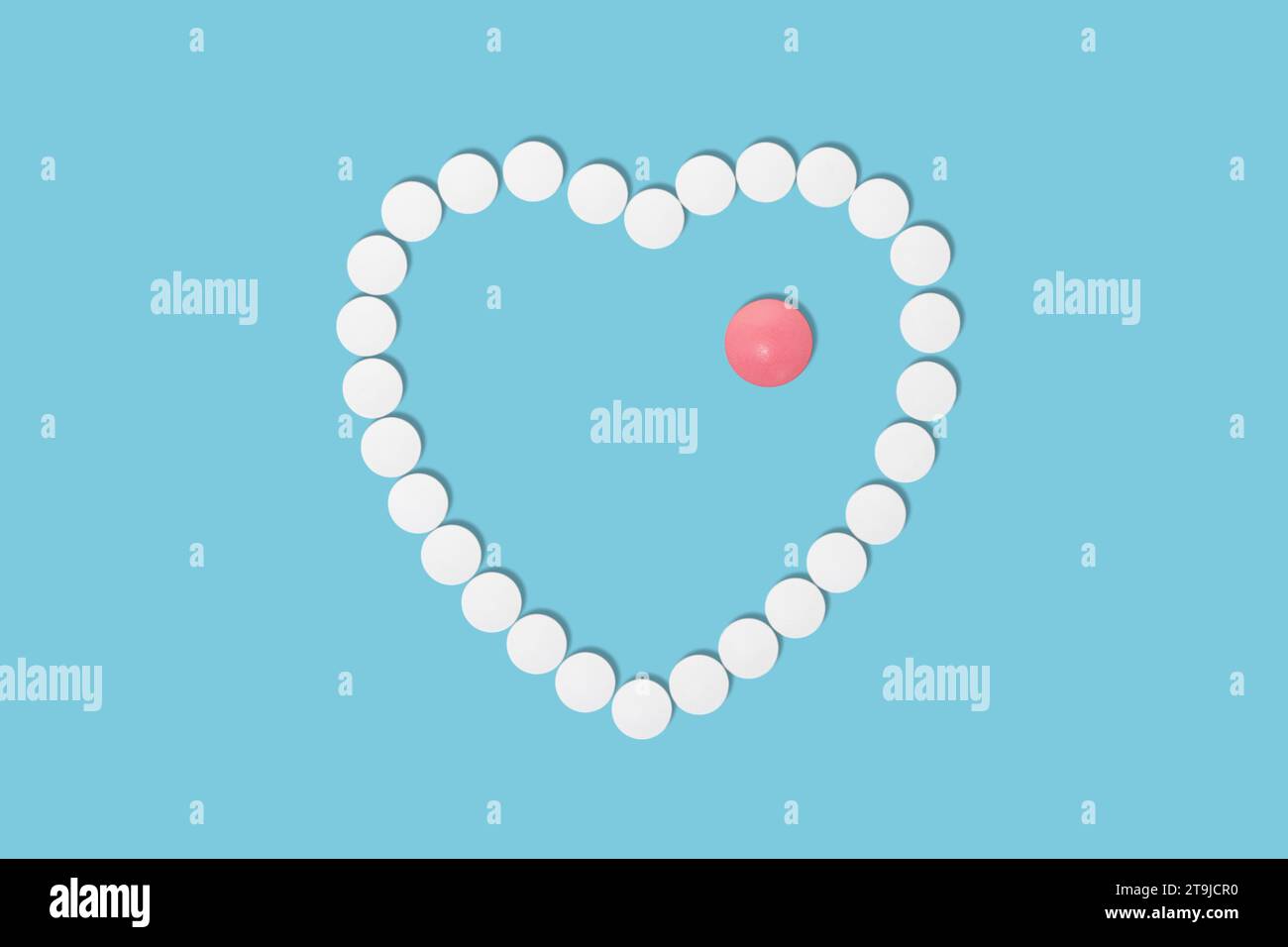 White round pills create a heart shape on a blue background and a red ...