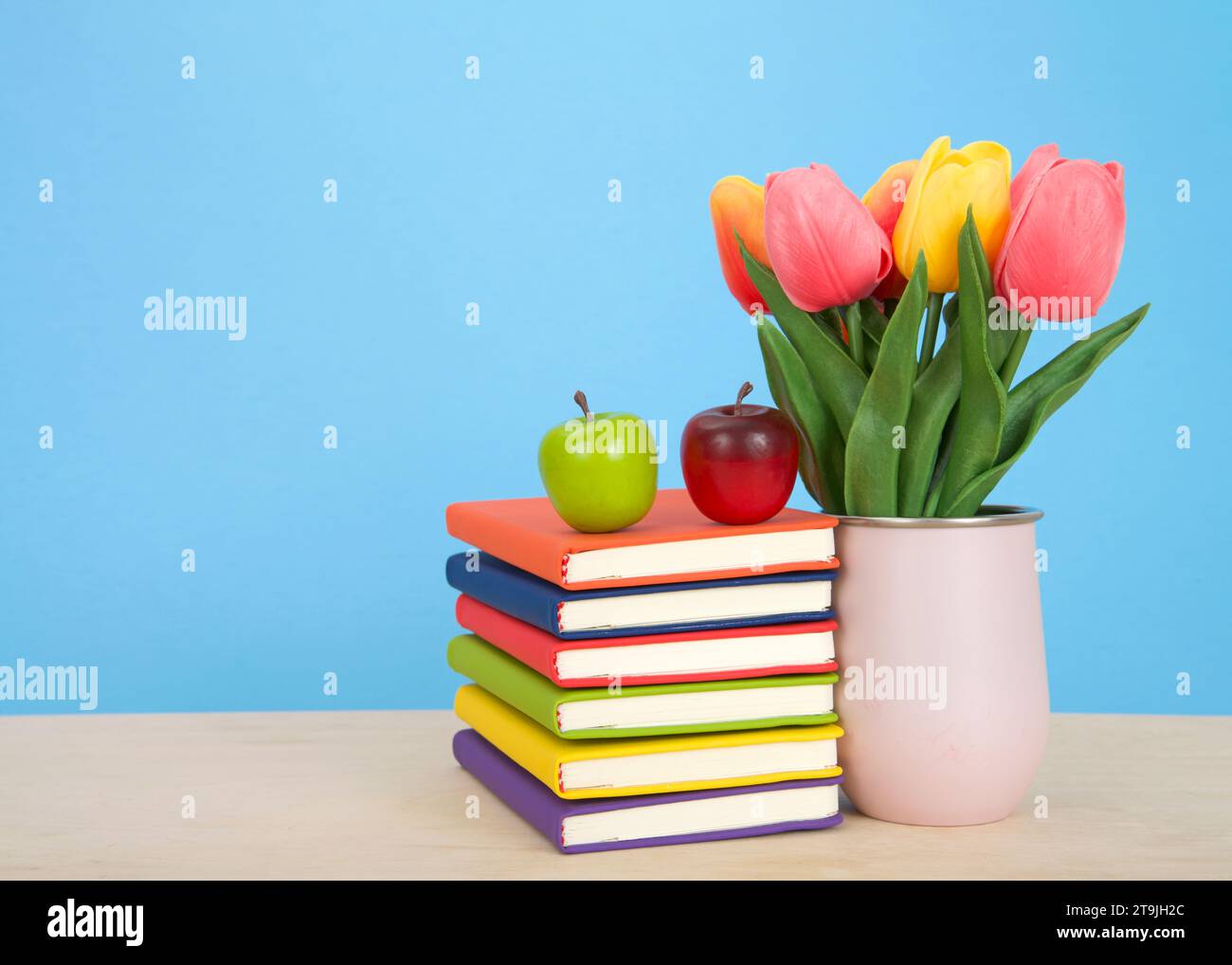 Bright colorful bound books stacked on a light wood table with blue ...