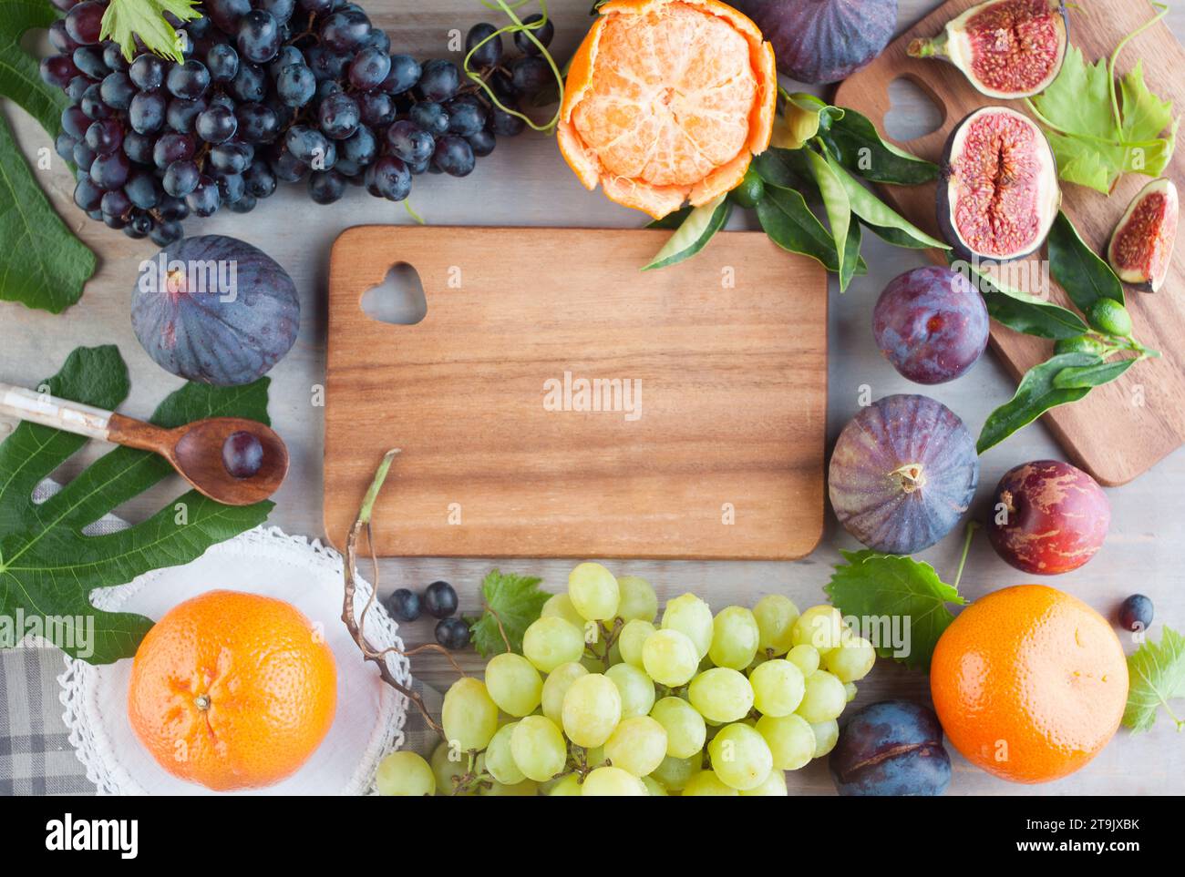 Bright orange tangerine, green leaves, grape, plum and figs with empty ...