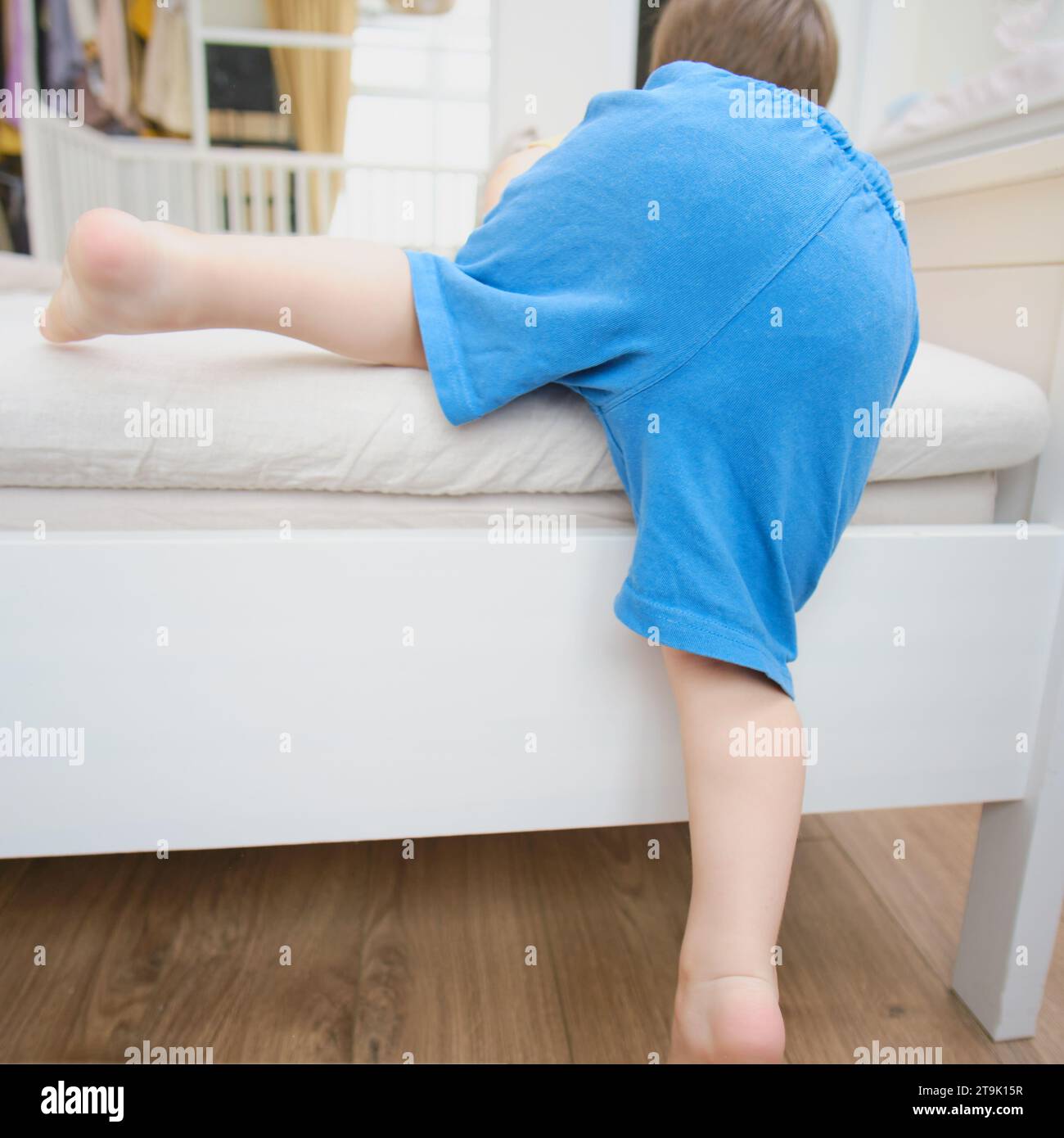 The baby is climbing on a high bed, risking an indoor accident. Kid ...