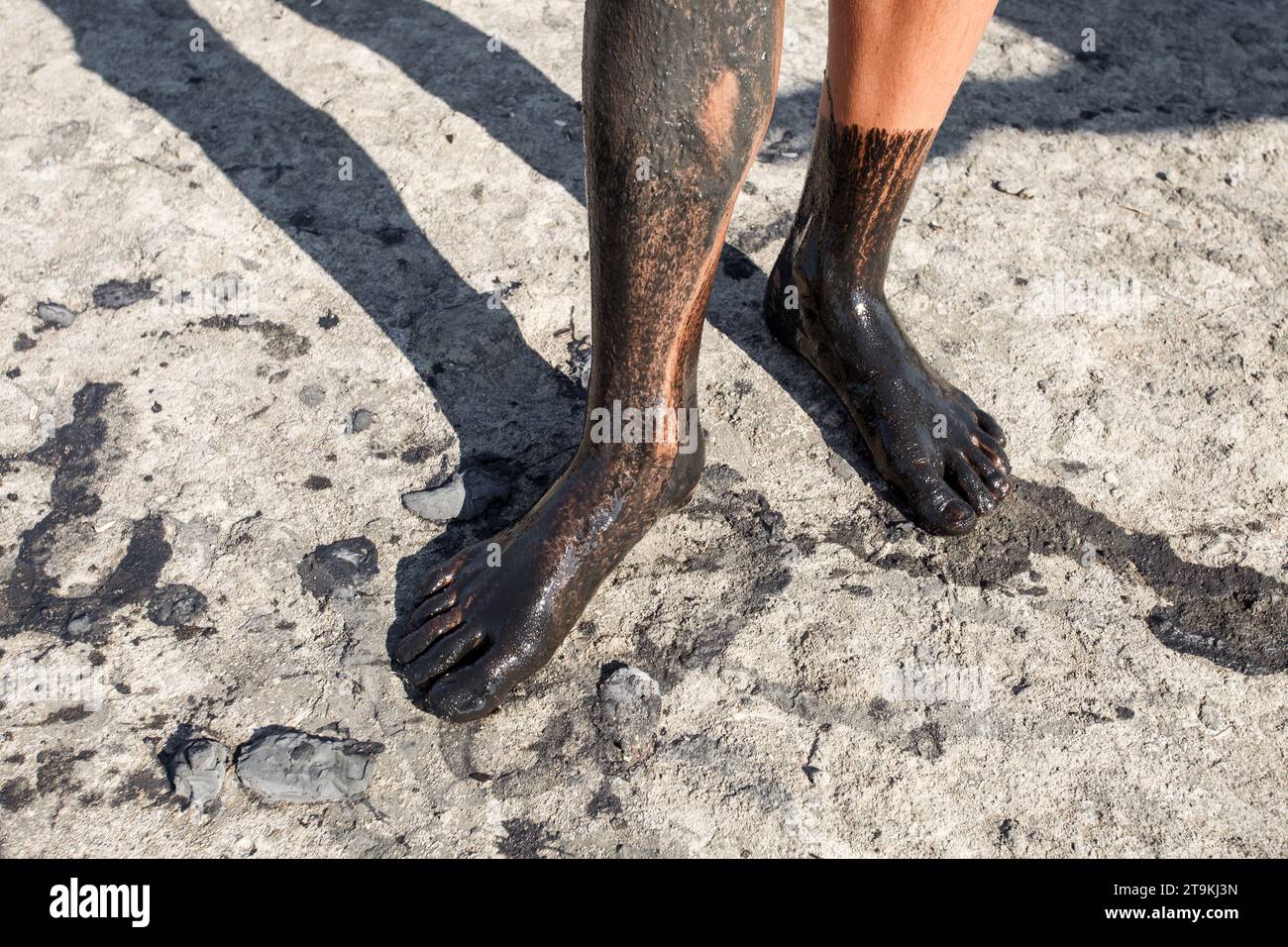 Feet of child's boy, smeared in therapeutic mud, standing on dried soil ...