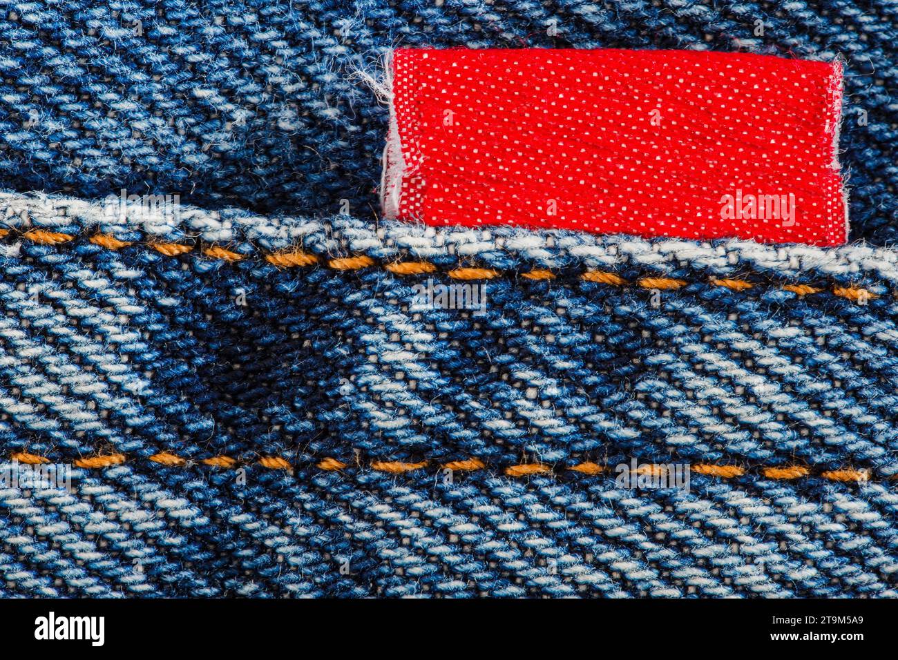 Jeans fabric, seam with orange threads and red sewn label, close-up ...
