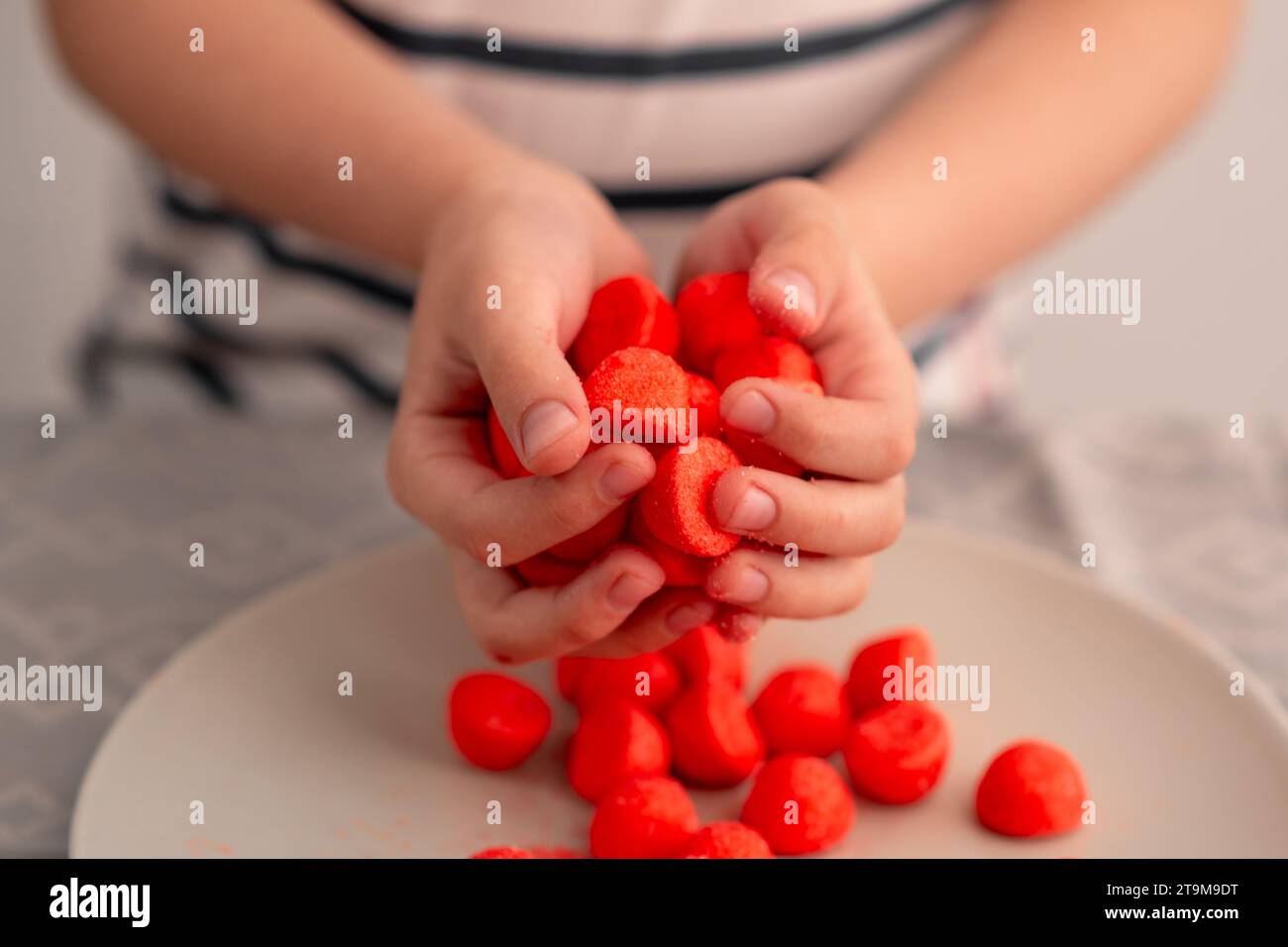 Sweet indulgence in the hands of a child red fruity candies on a plate ...