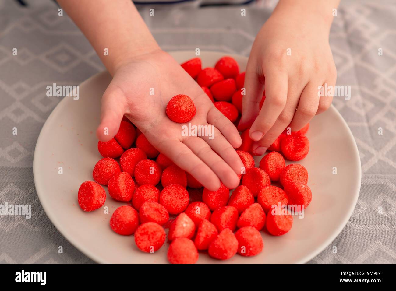 Sweet moments unfold as a child's hands eagerly grasp red fruit candies ...