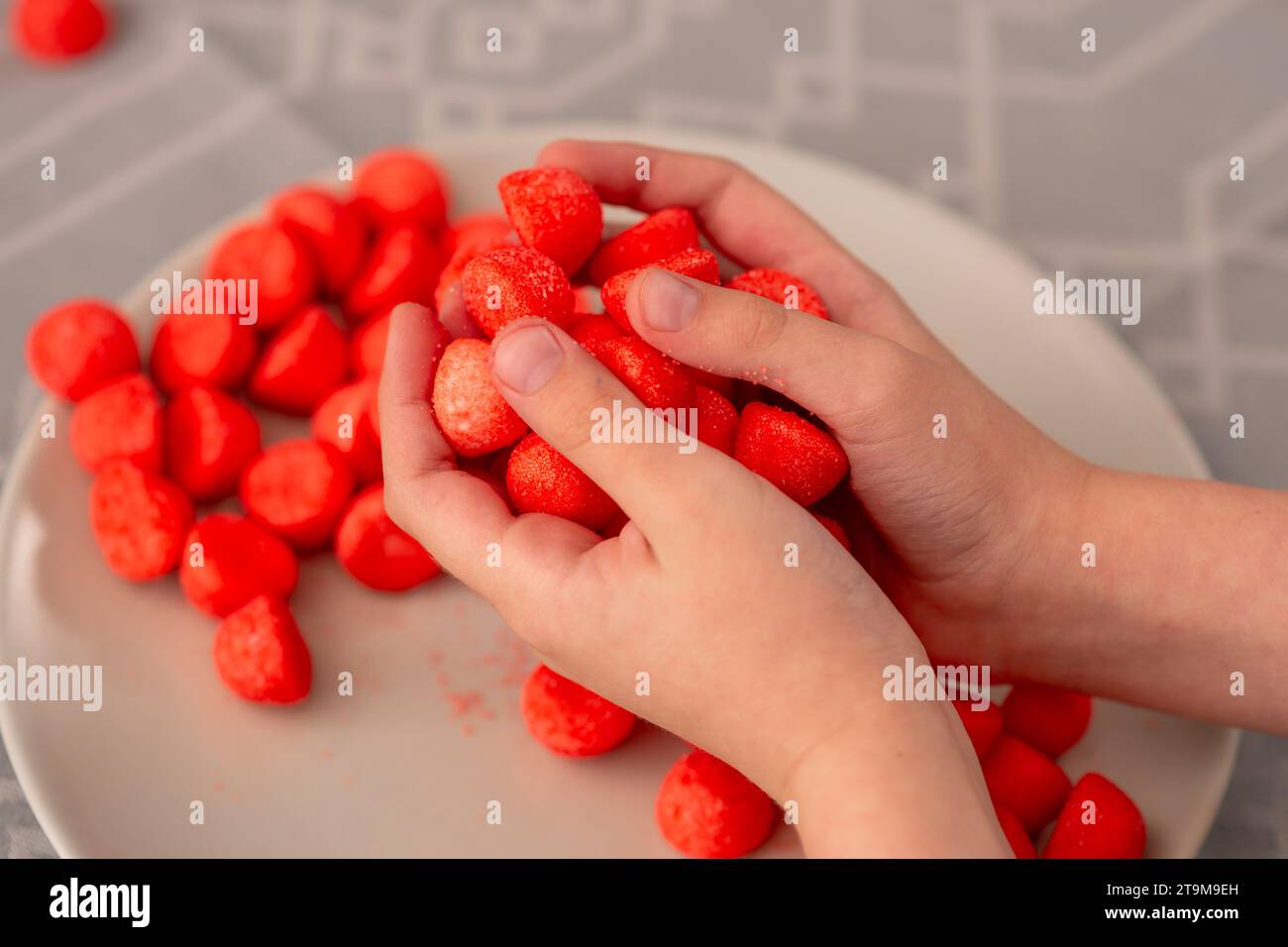 Sweet indulgence in the hands of a child red fruity candies on a plate ...