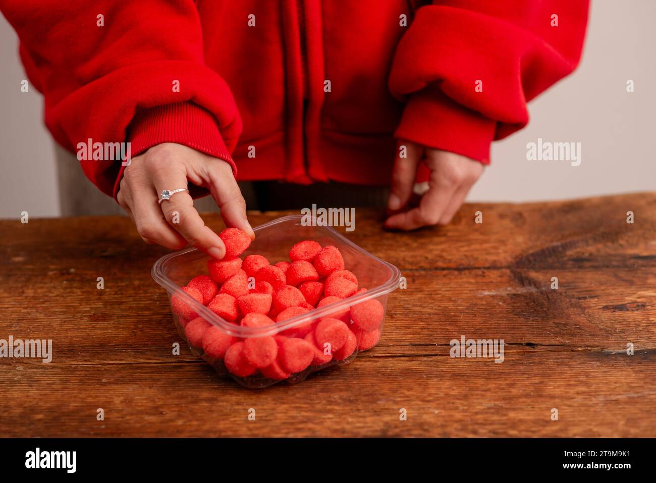 Sweet indulgence: Woman's hands hold red chewy candies against a wooden ...