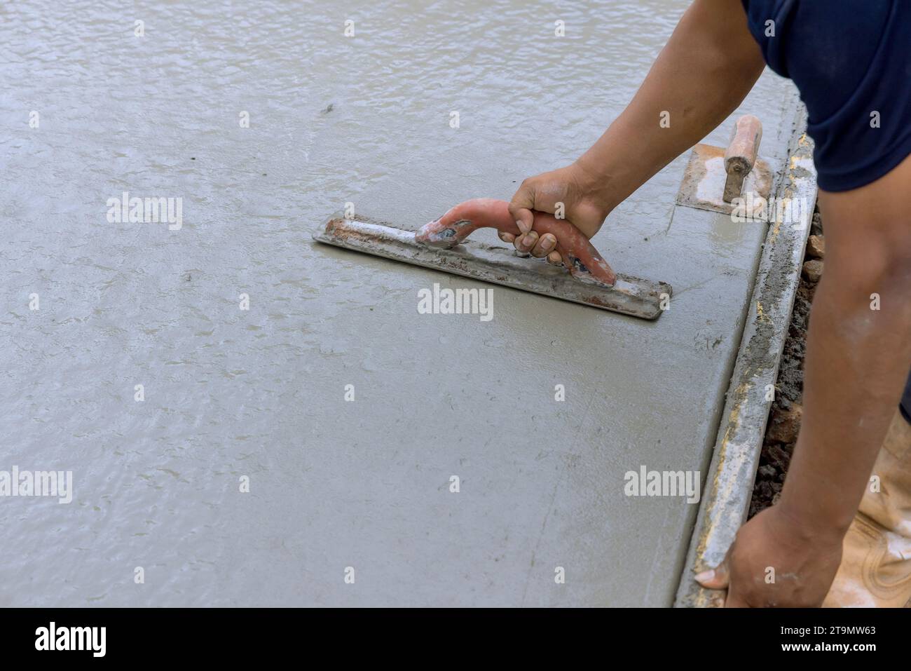Builder mason worker leveling fresh concrete pavement wet cement using ...