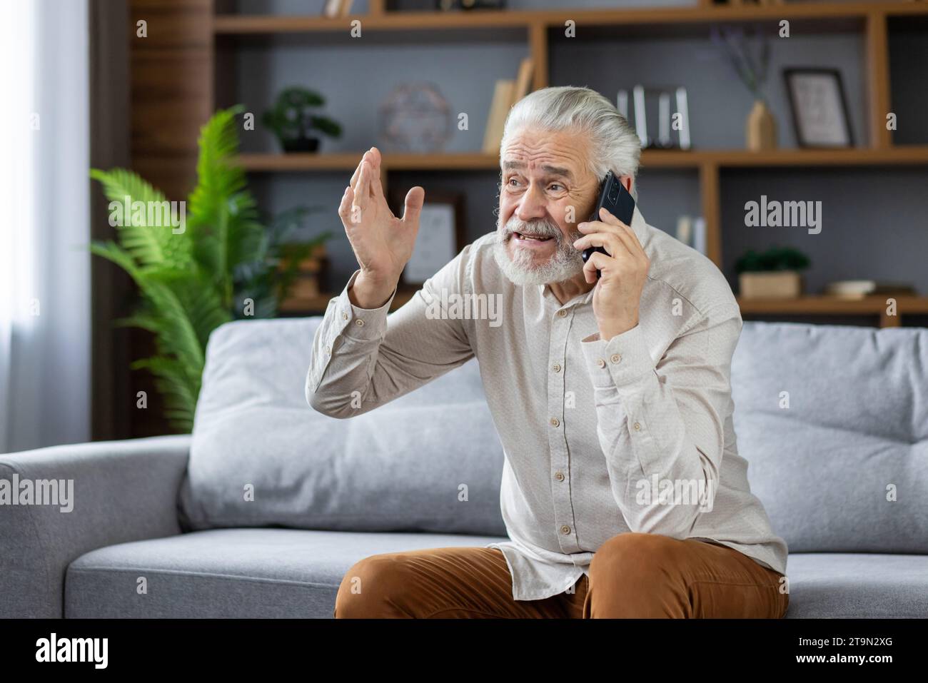 Upset and angry senior man talking on the phone at home, sitting on the ...