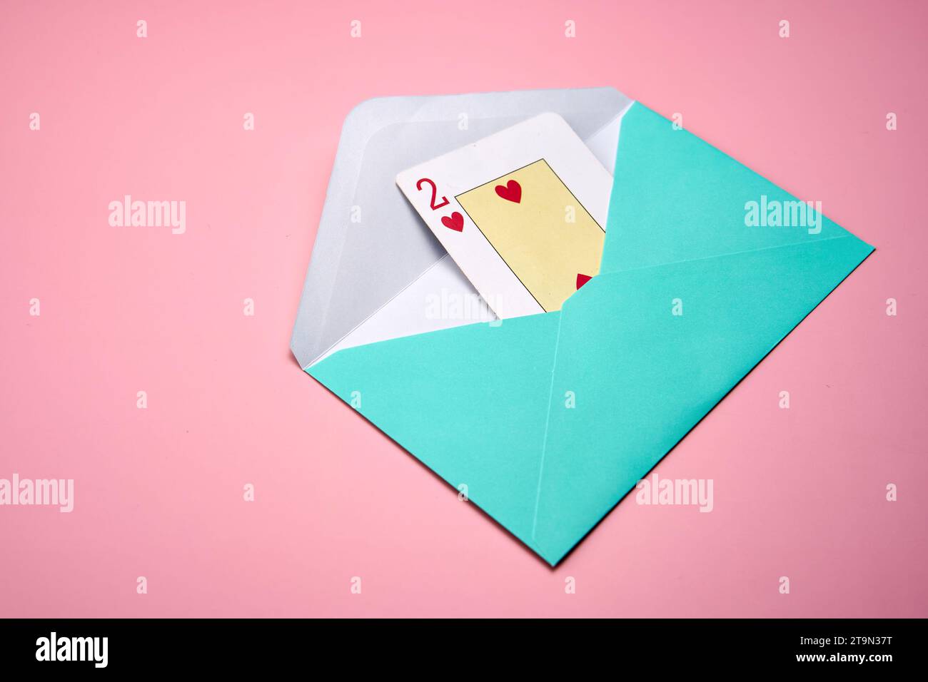 Two hearts playing card inside a blue envelope on a pink background ...