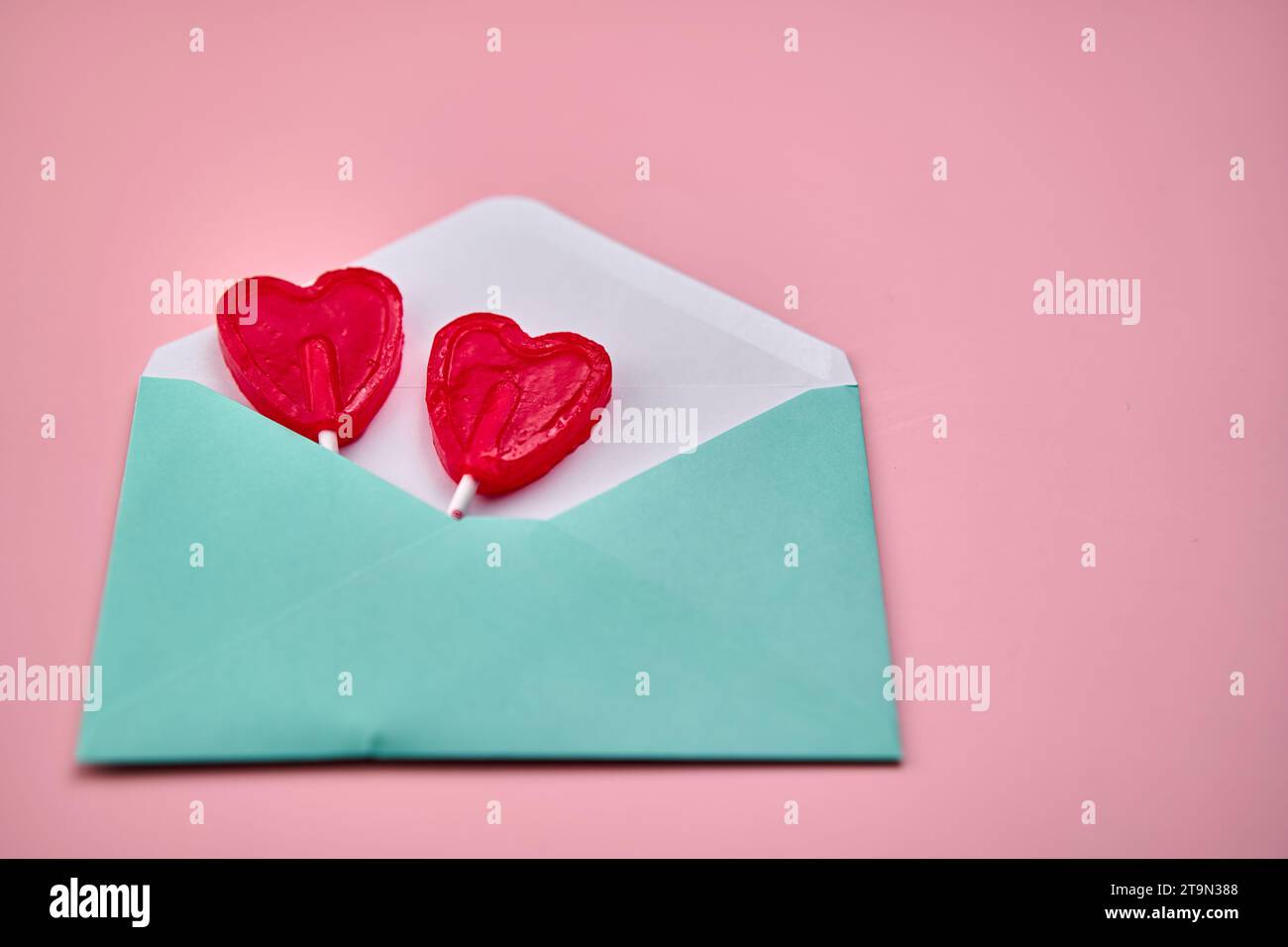 Love letter with two heart-shaped red lollipops inside on a pink ...