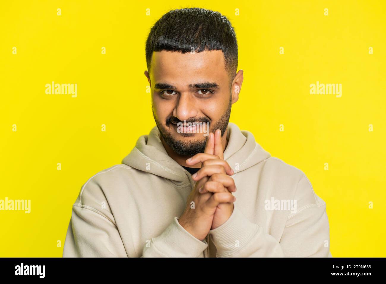 Sneaky cunning Indian young man with tricky face gesticulating and scheming evil plan thinking ...