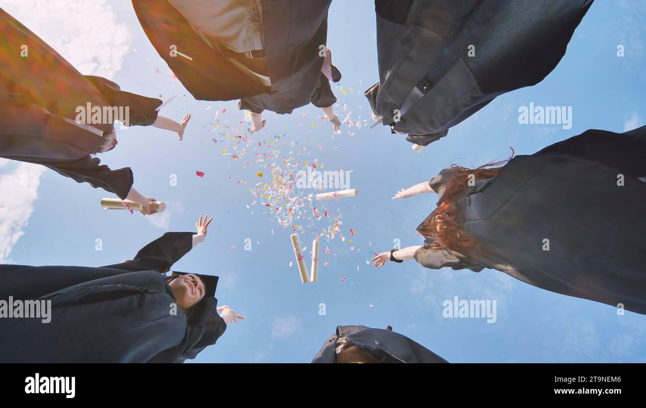 Happy graduates throwing up colorful confetti against the blue summer ...