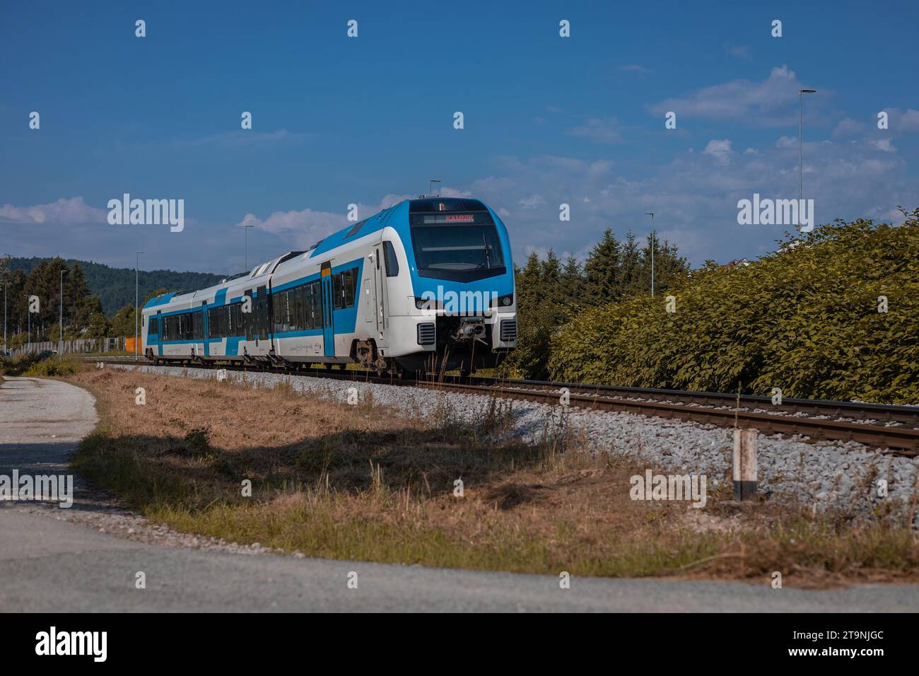 Blue and white modern passenger train is closing to a station on local ...