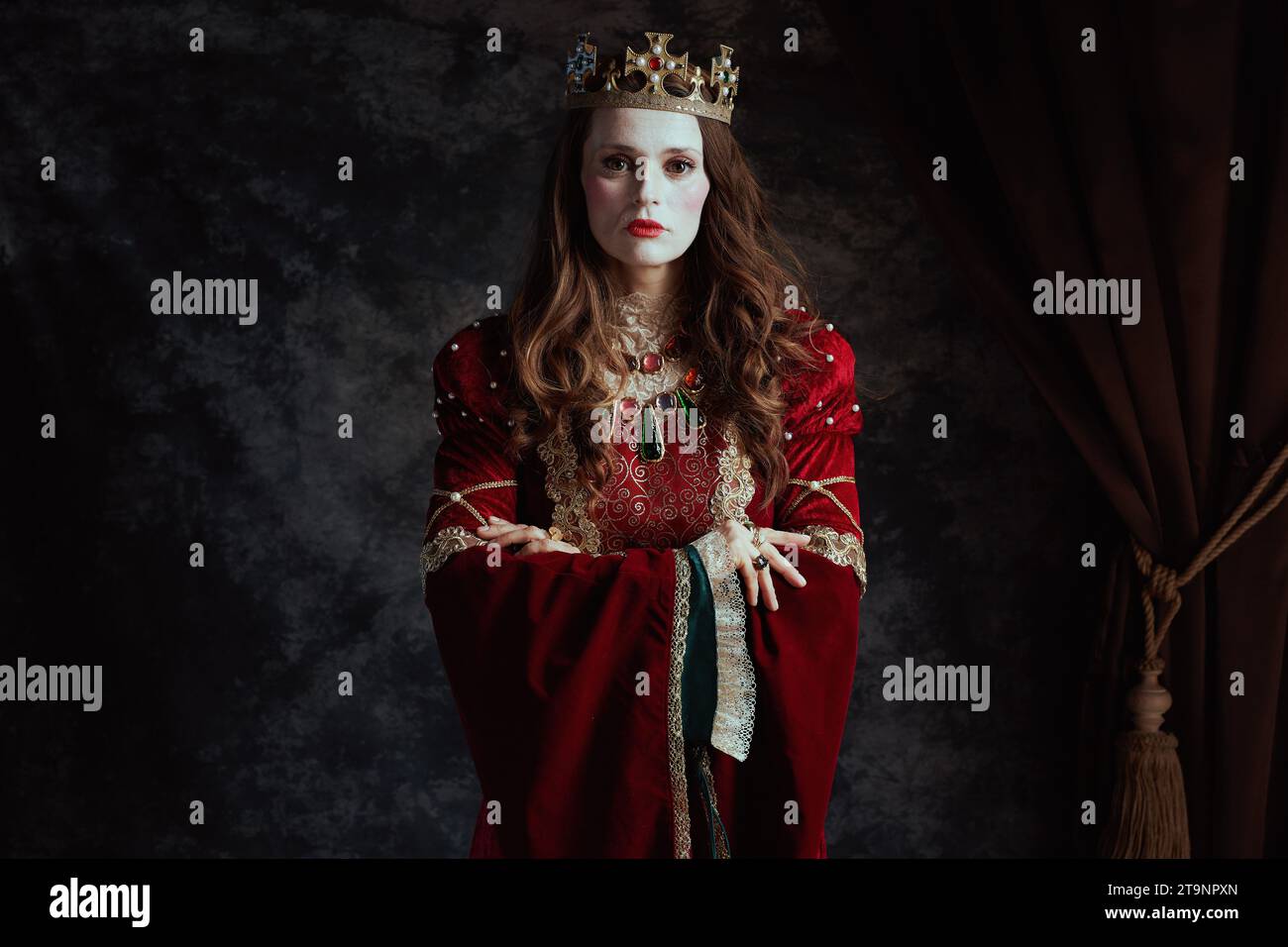 medieval queen in red dress with white makeup and crown on dark gray ...