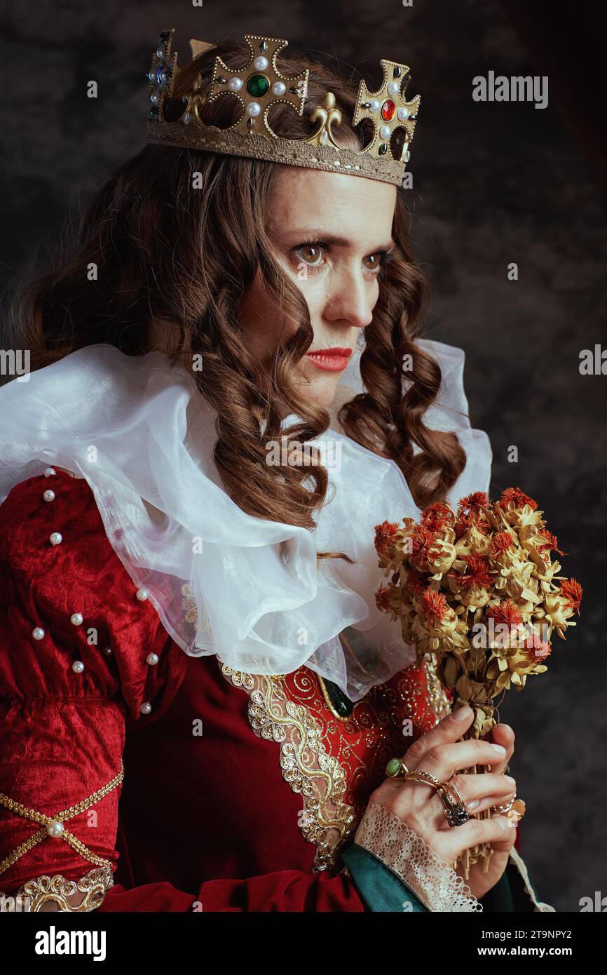 sad medieval queen in red dress with dried flower, white collar and ...