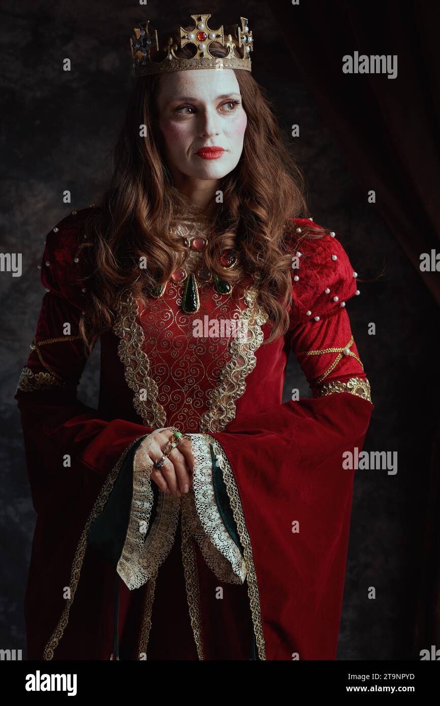medieval queen in red dress with white makeup and crown on dark gray ...