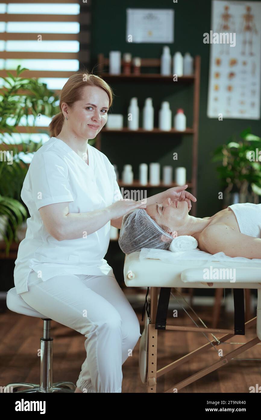 Healthcare time. massage therapist in massage cabinet massaging clients face on massage table ...