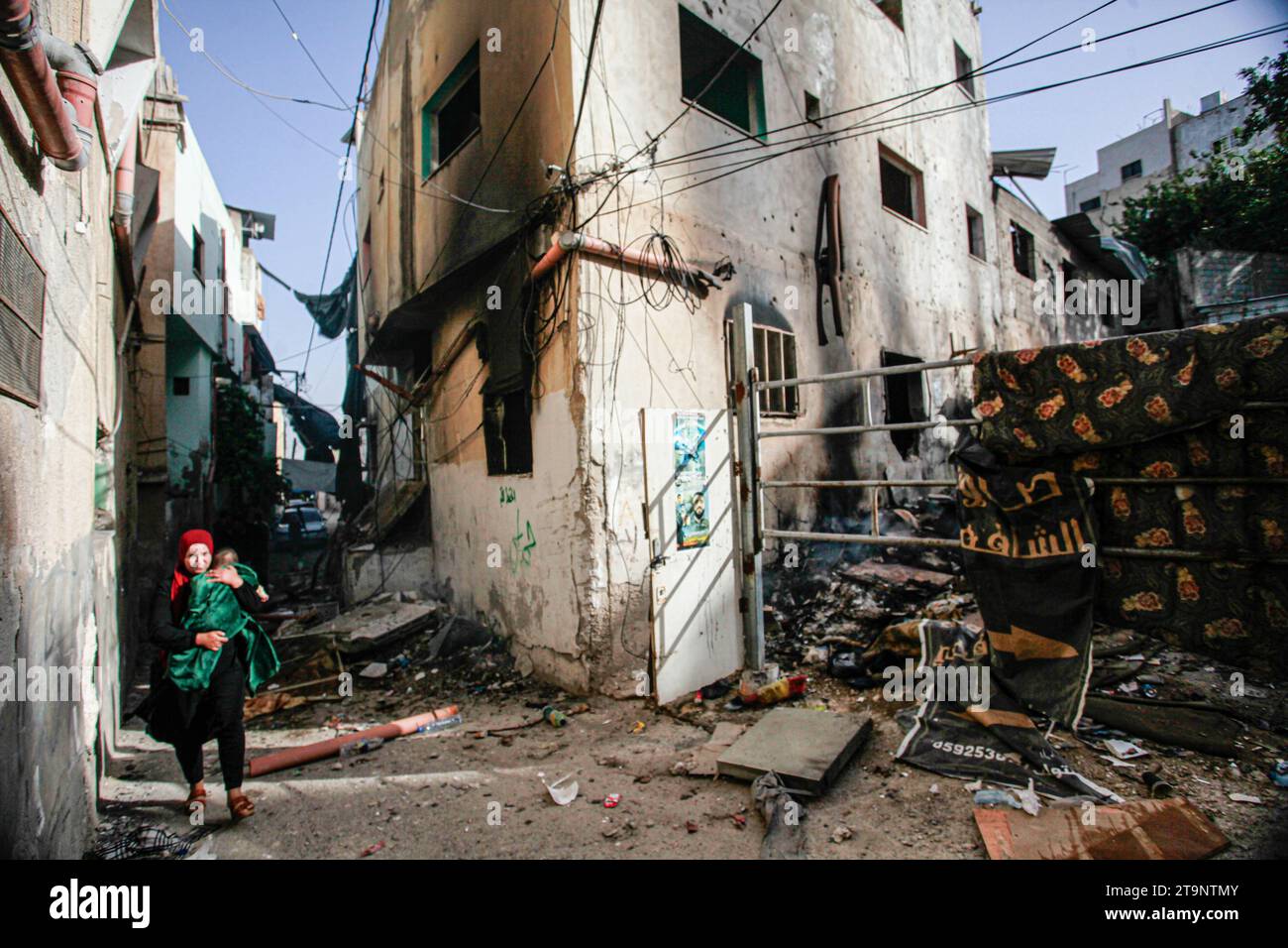 Jenin, Palestine. 26th Nov, 2023. A woman carrying a child walks ...