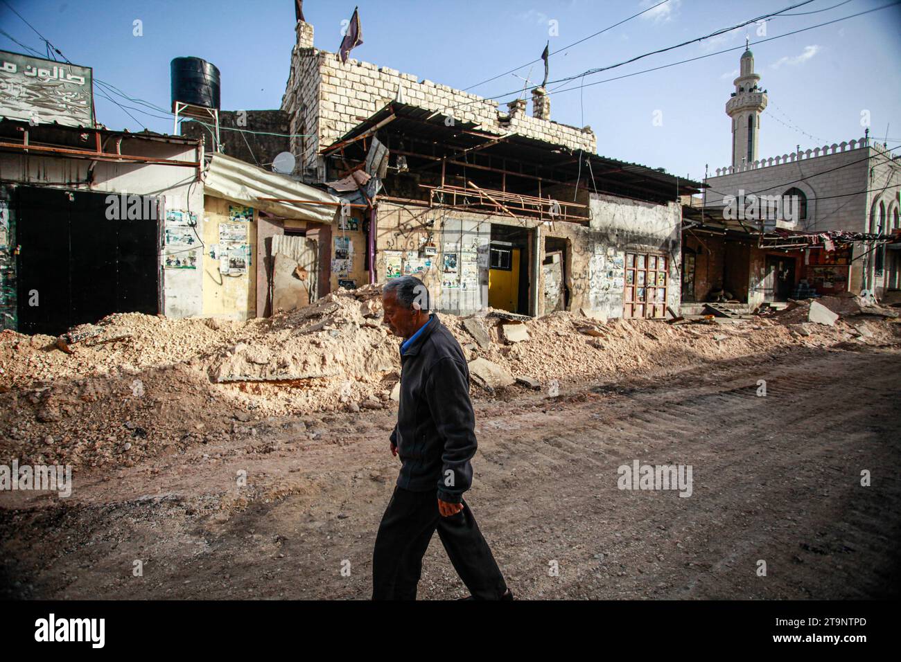 Jenin, Palestine. 26th Nov, 2023. A man walks past damaged buildings ...