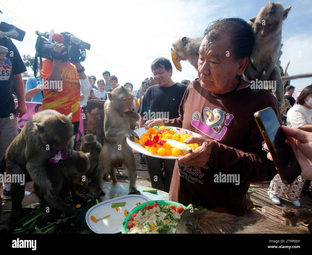 Monkeys eat fruit as they cling onto Yongyuth Kitwatananusont who ...