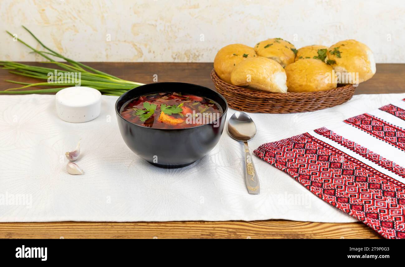 A plate of borsch and pampushka buns with garlic and herbs on a Ukrainian-style table with an ...