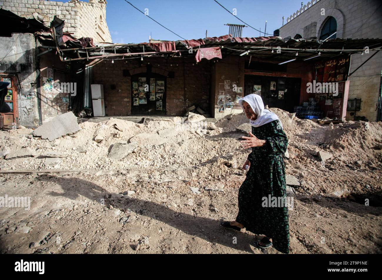 Jenin, Palestine. 26th Nov, 2023. A woman walks past damaged buildings ...
