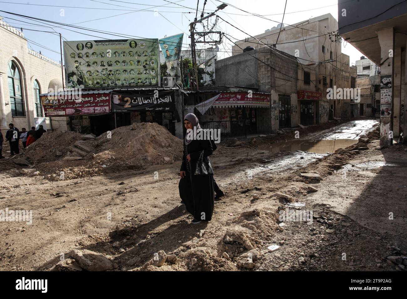 Jenin, Palestine. 26th Nov, 2023. A woman walks past damaged buildings ...