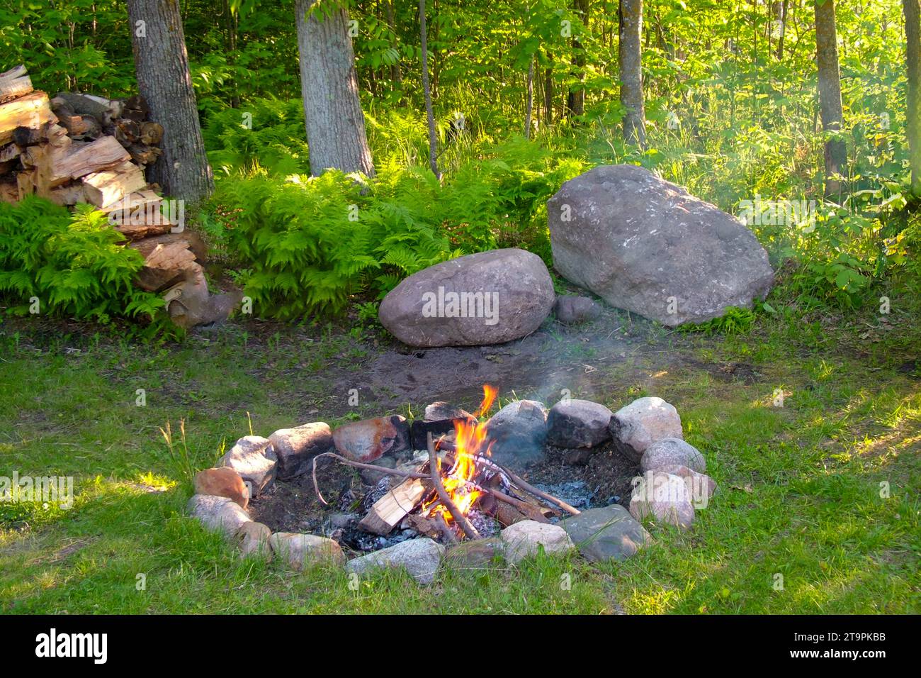 Campfire in stone fire ring/pit, cut camp wood, with large boulders as ...