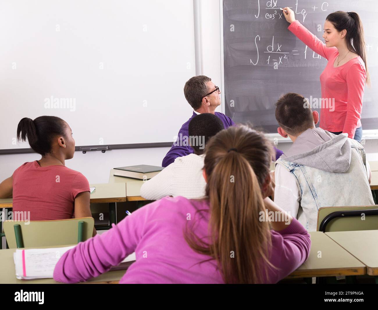 Cute student girl solves task near blackboard in classroom mathematics ...