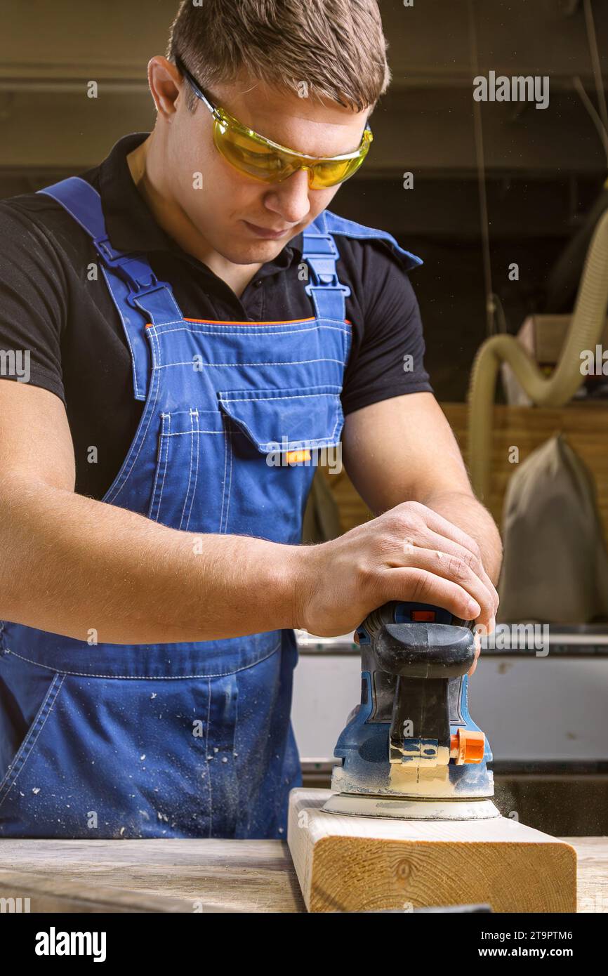 Portrait of a young man carpenter using electric sanding machine to ...