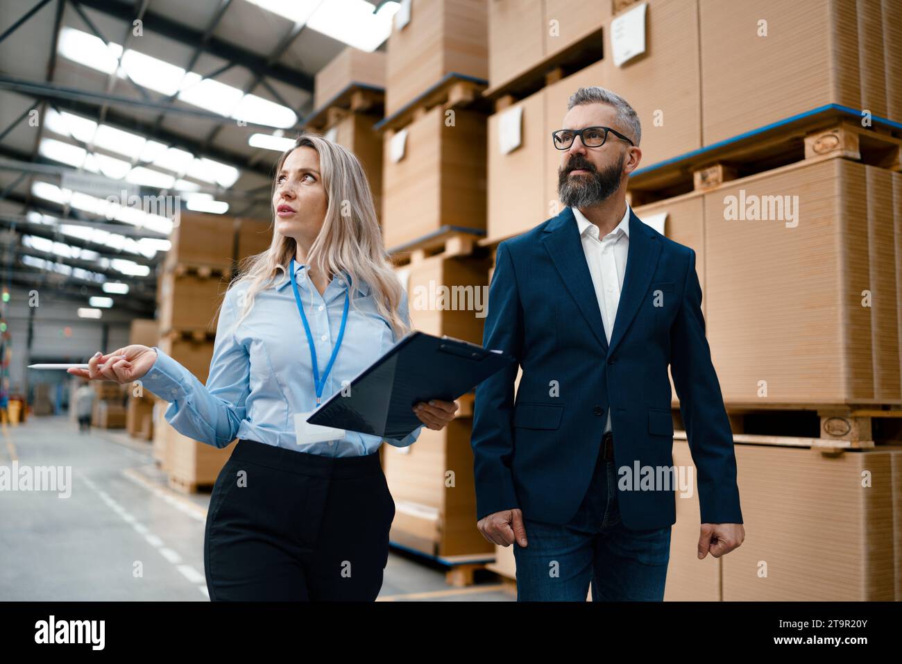 Female warehouse manager talking with logistics employee in warehouse ...