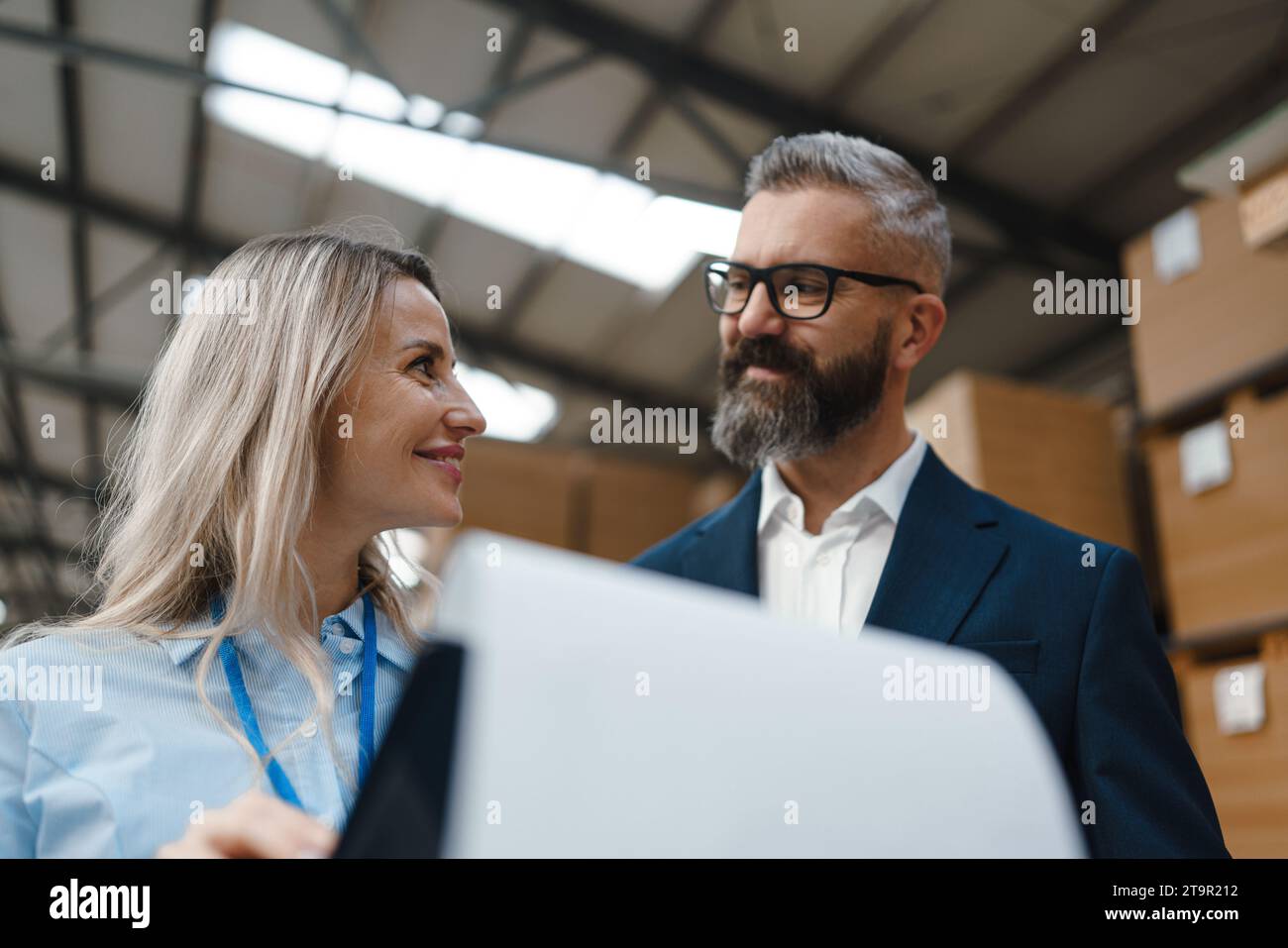 Female warehouse manager talking with logistics employee in warehouse ...