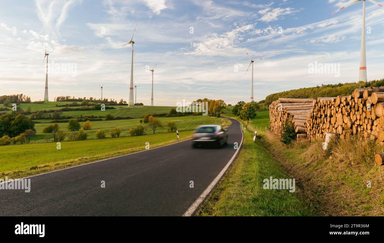A car driving through a rural area with wind turbines and cut wood in ...