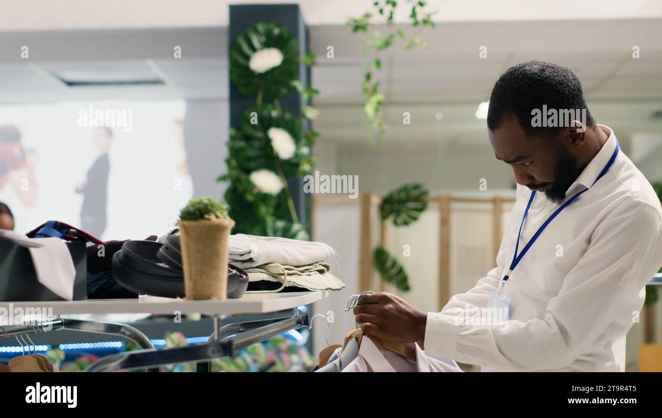 Elegant worker arranging clothes in mall clothing store with fast ...