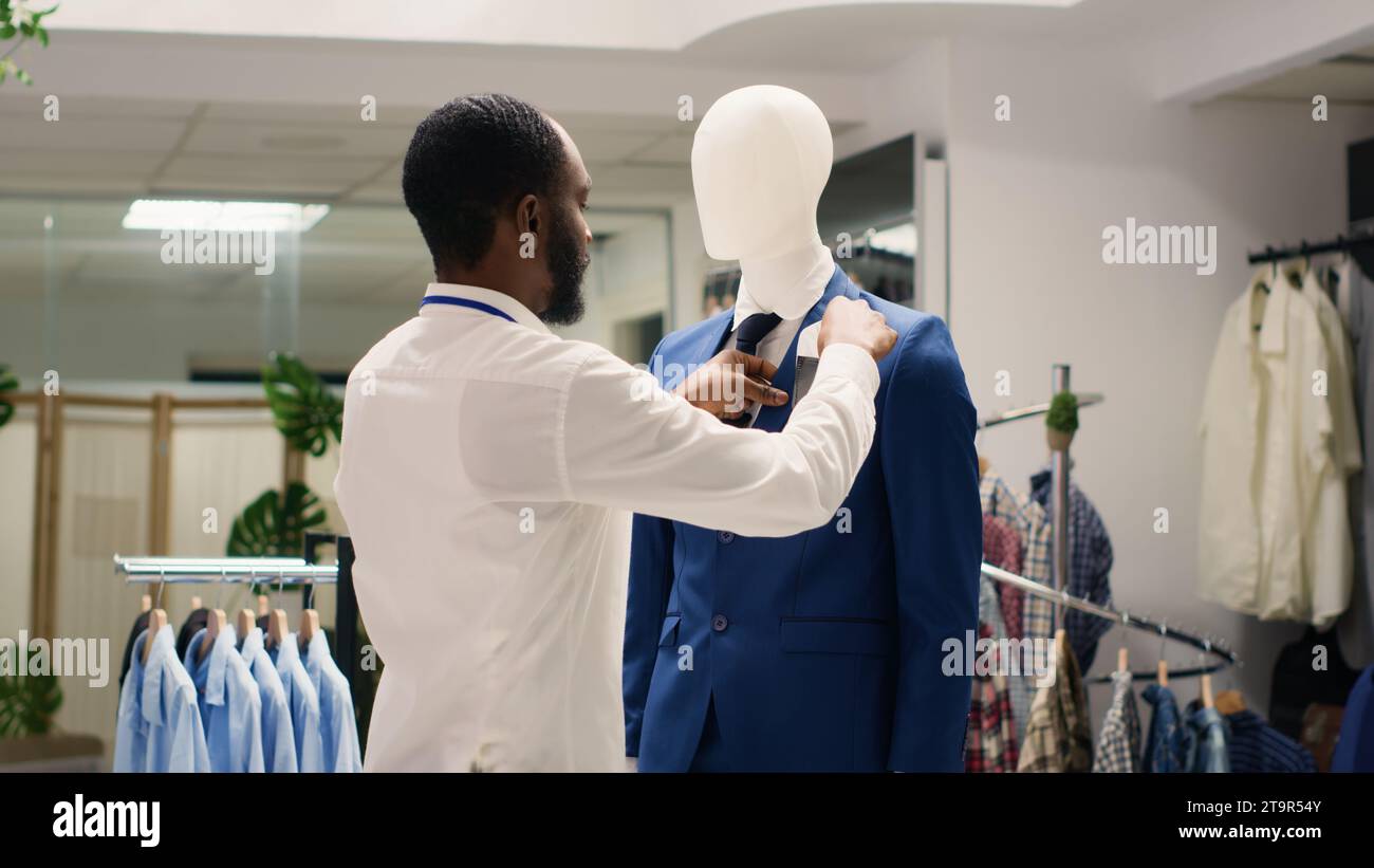 Stylish employee arranging elegant clothes on mannequins in luxurious ...