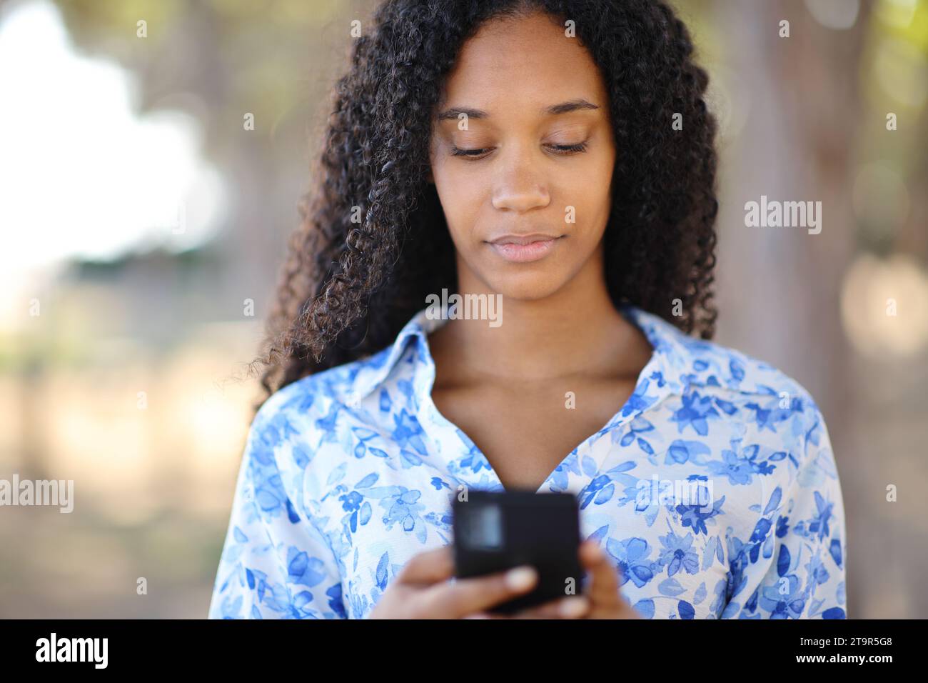 Front view of a serious black woman using cell phone in a park Stock ...