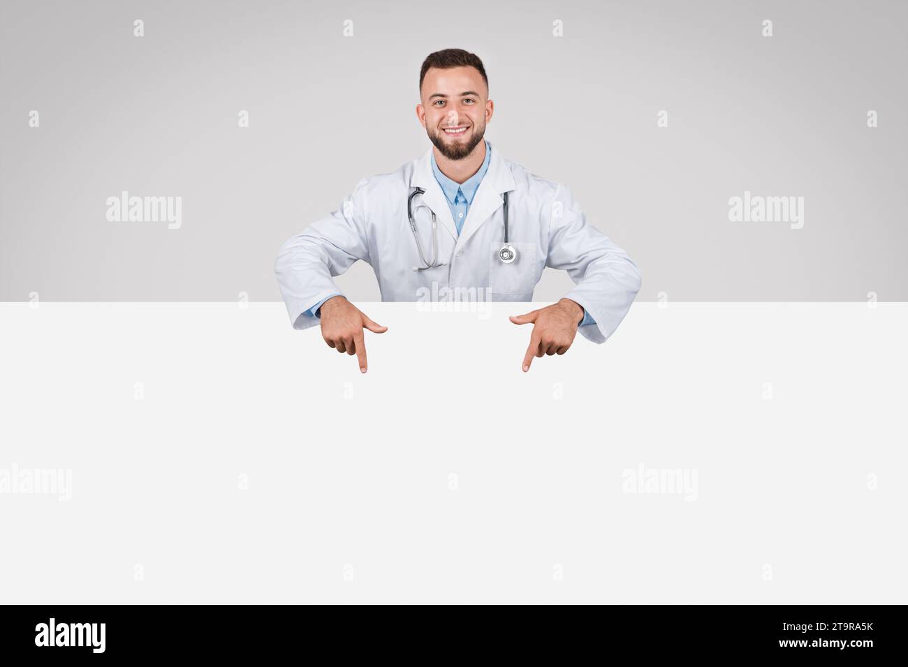 Doctor man pointing at empty white board below, grey background Stock ...