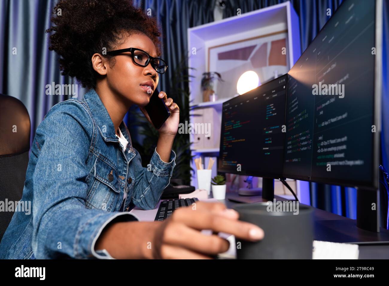 Working young African IT developer smartphone calling and discussing with friend, wearing jeans ...