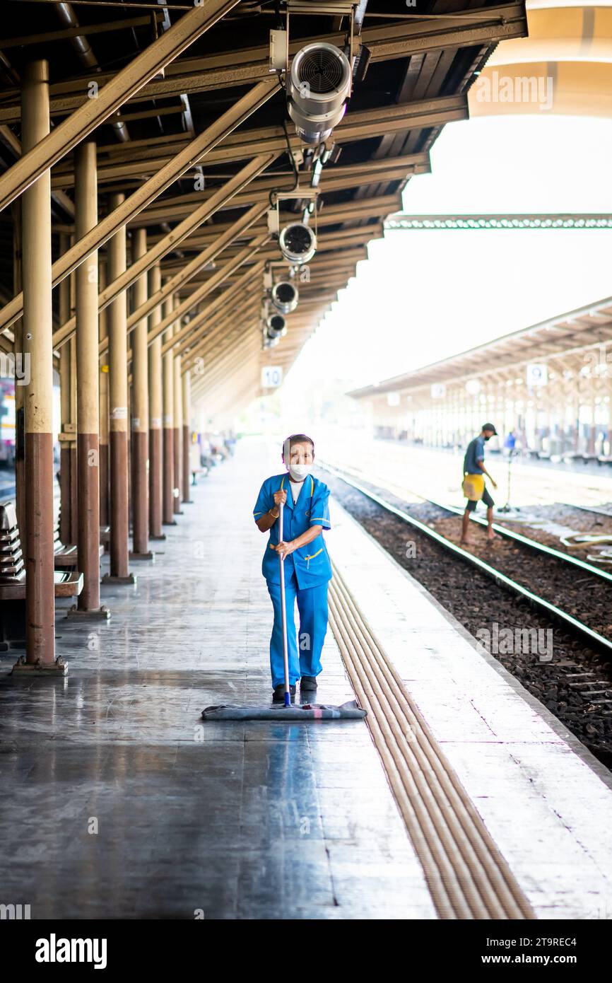 A female Thai cleaner makes her way along the platform mopping and ...
