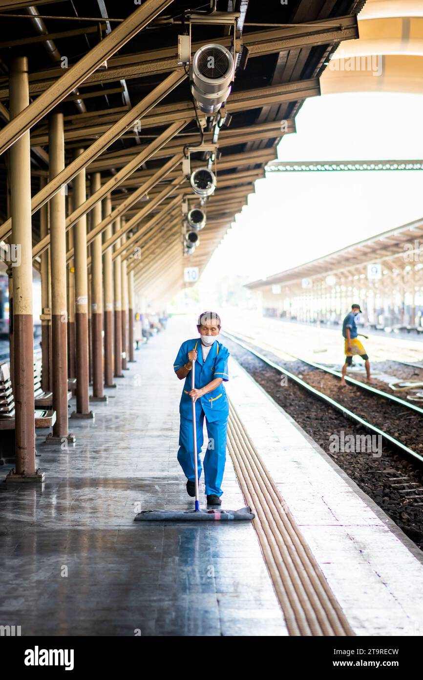 A female Thai cleaner makes her way along the platform mopping and ...