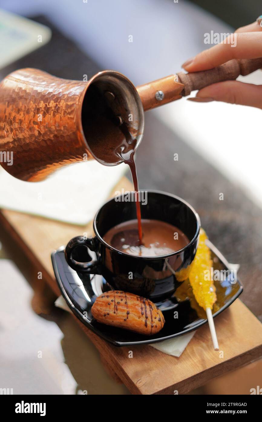 Coffee pouring from a Turkish copper coffee pot into a black coffee cup ...