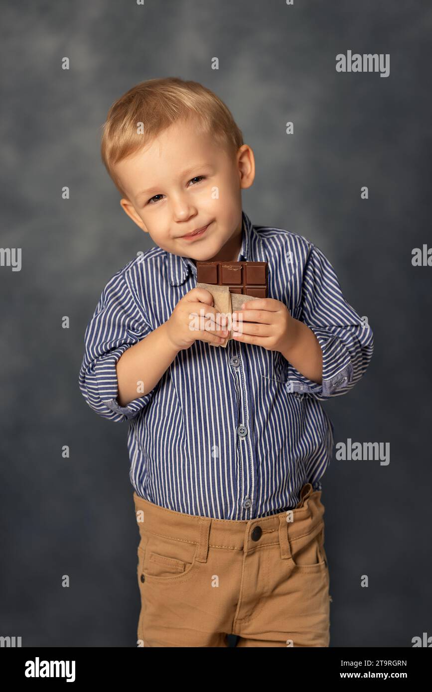 Portrait of a small boy kid eating chocolate on grey background. Happy ...