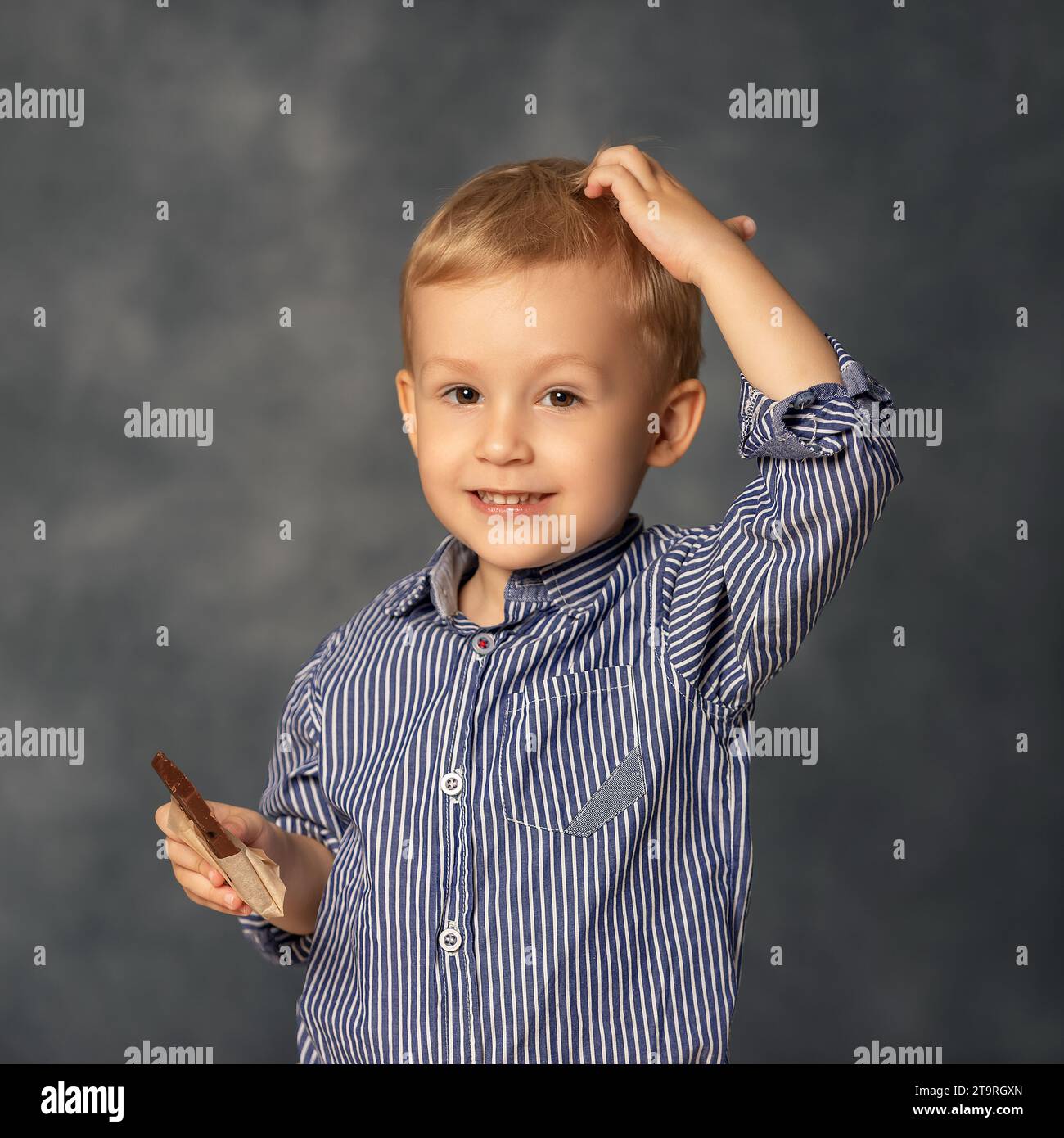 Portrait of a small boy kid eating chocolate on grey background. Happy ...