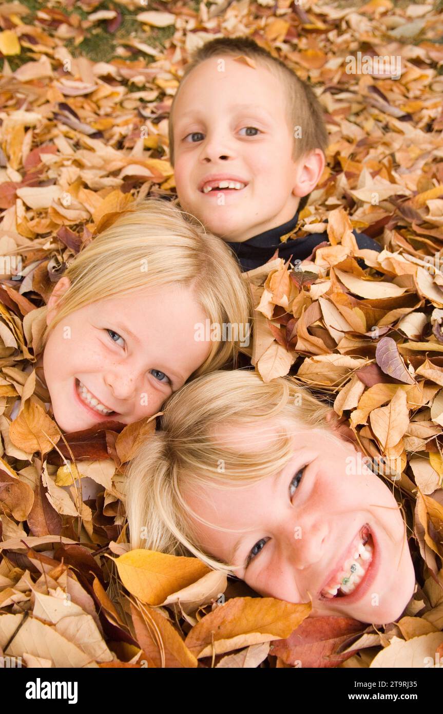 Three kids, two girls and one boy, play in the fall leaves in Fort ...