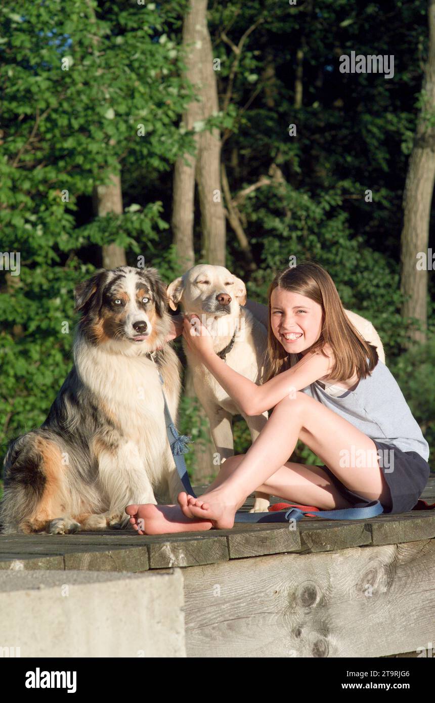 A girl sits with her two dogs on a deck Stock Photo - Alamy
