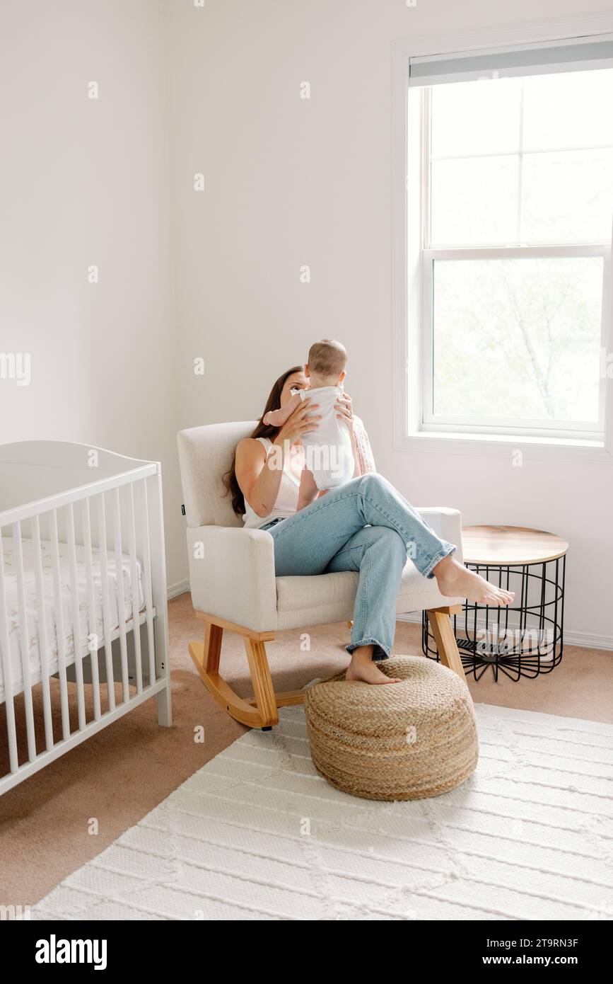 Mom sitting on rocking chair in neutral nursery holding baby Stock ...