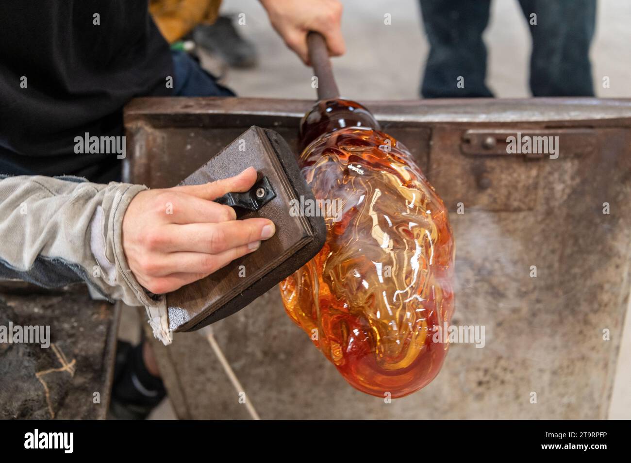 A glassblower skilfully shapes a heated molten mould of clear glass ...
