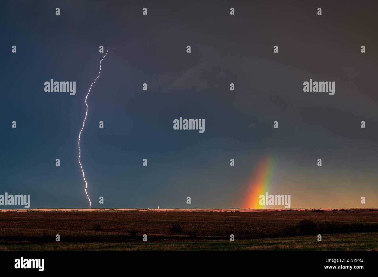 A rainbow and a brilliant lightning bolt streaks across the sky above ...