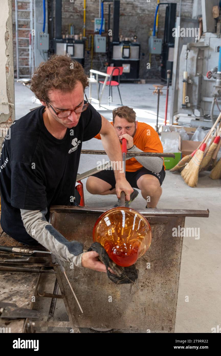 A glassblower skilfully shapes a heated molten mould of clear glass ...